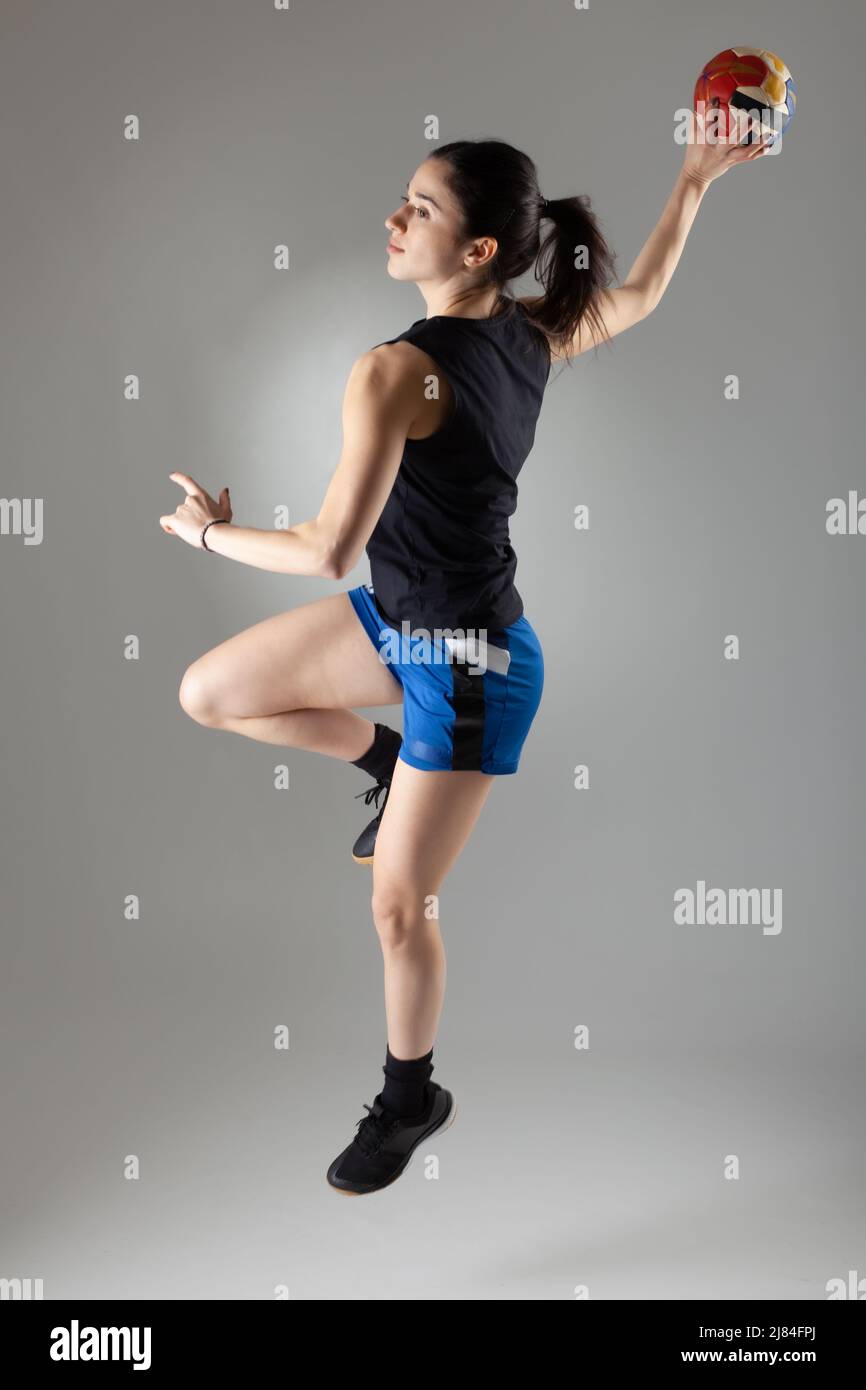 Handball player posing on light gray background. Girl jumping with ball ...