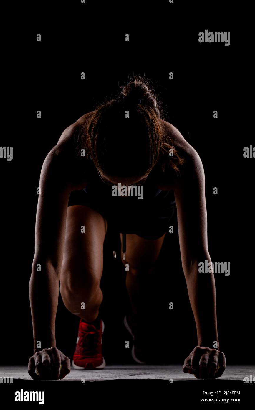 Side lit silhouette fit girl in race start position against dark ...