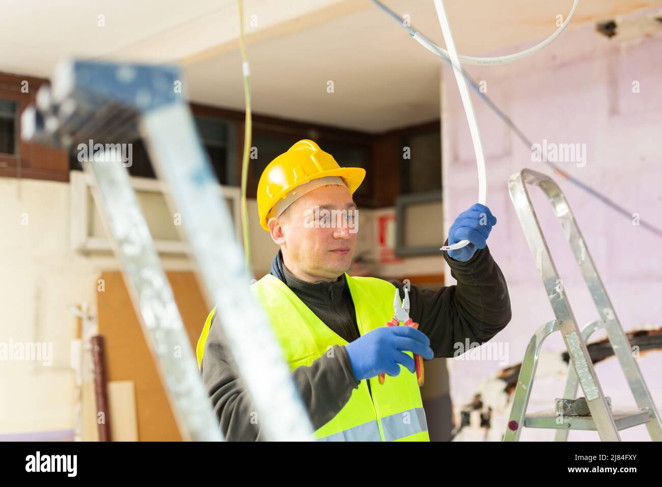 Electrician in protective uniform and helmet with pliers in his hands ...