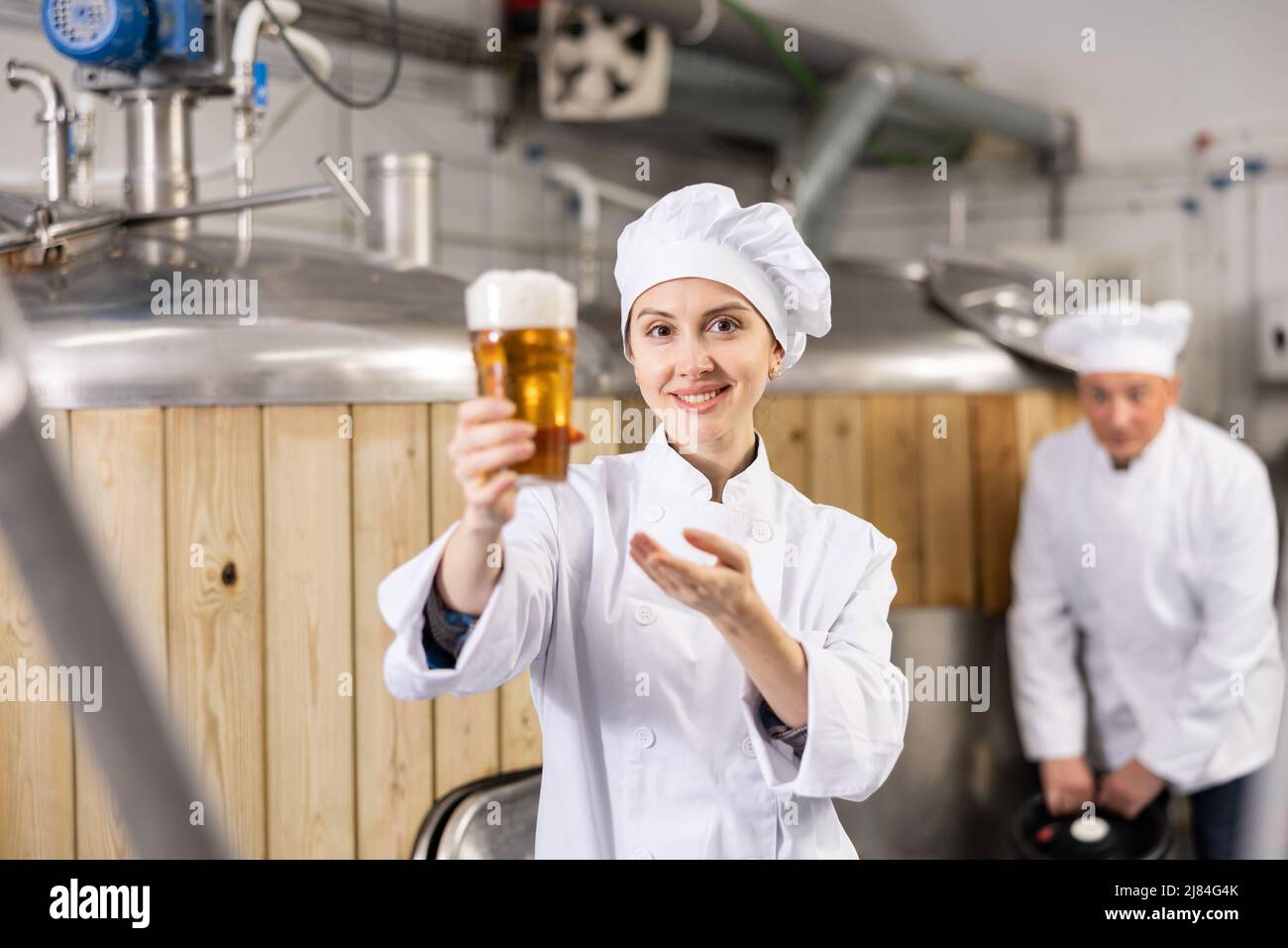 Female brewer is standing with beer with foam in glass on workplace ...