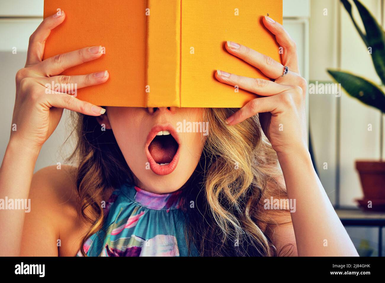 young shocked college woman with book in hands covering face library ...