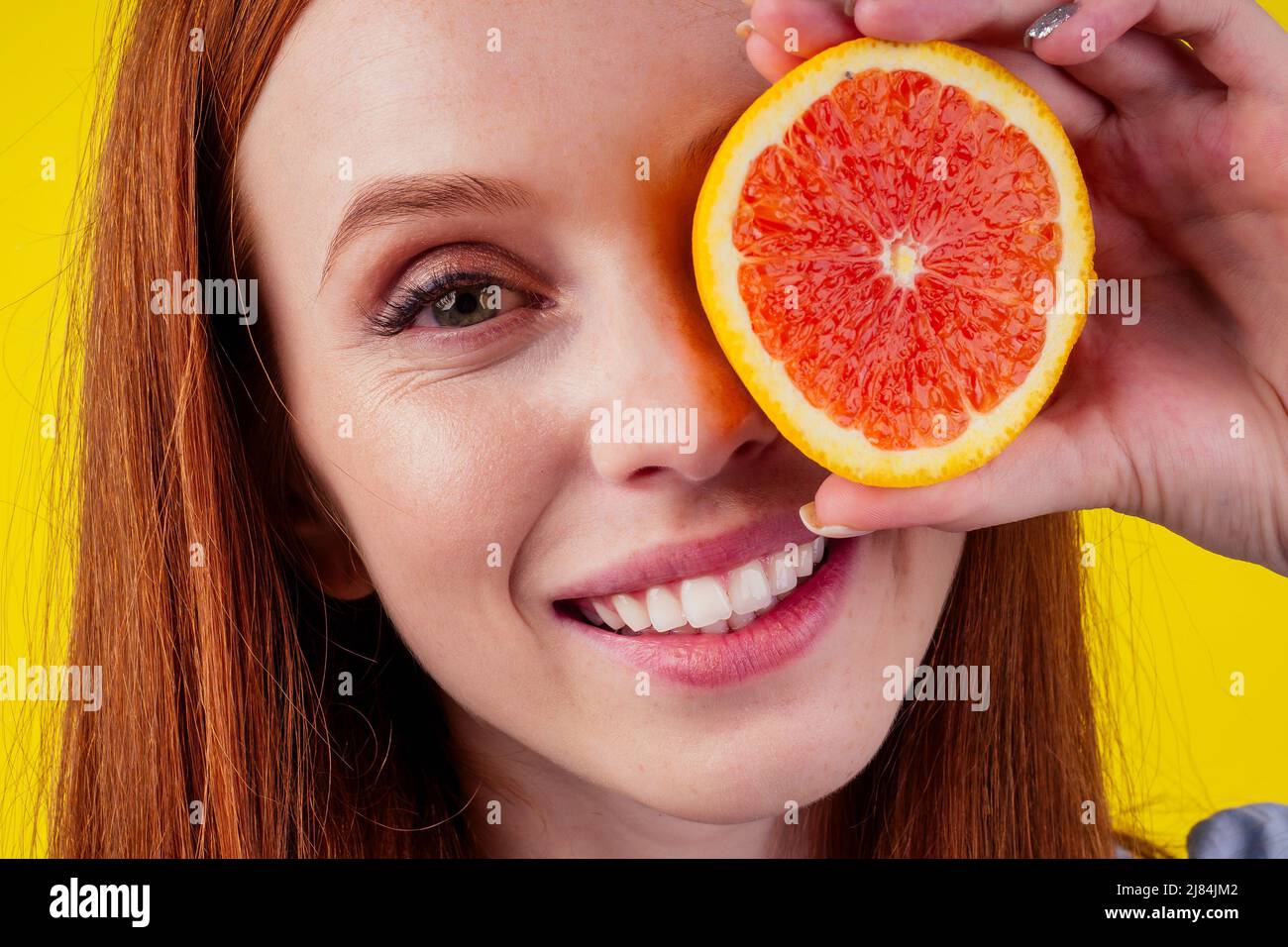 cheerful, redhaired ginger woman holding red hybrid orange in studio ...