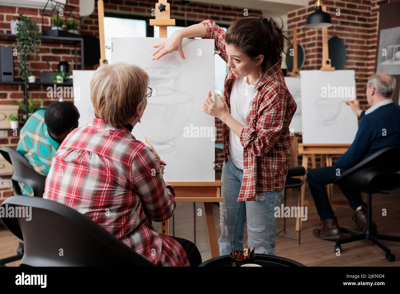 Art teacher helping senior student to develop sketching technique while ...