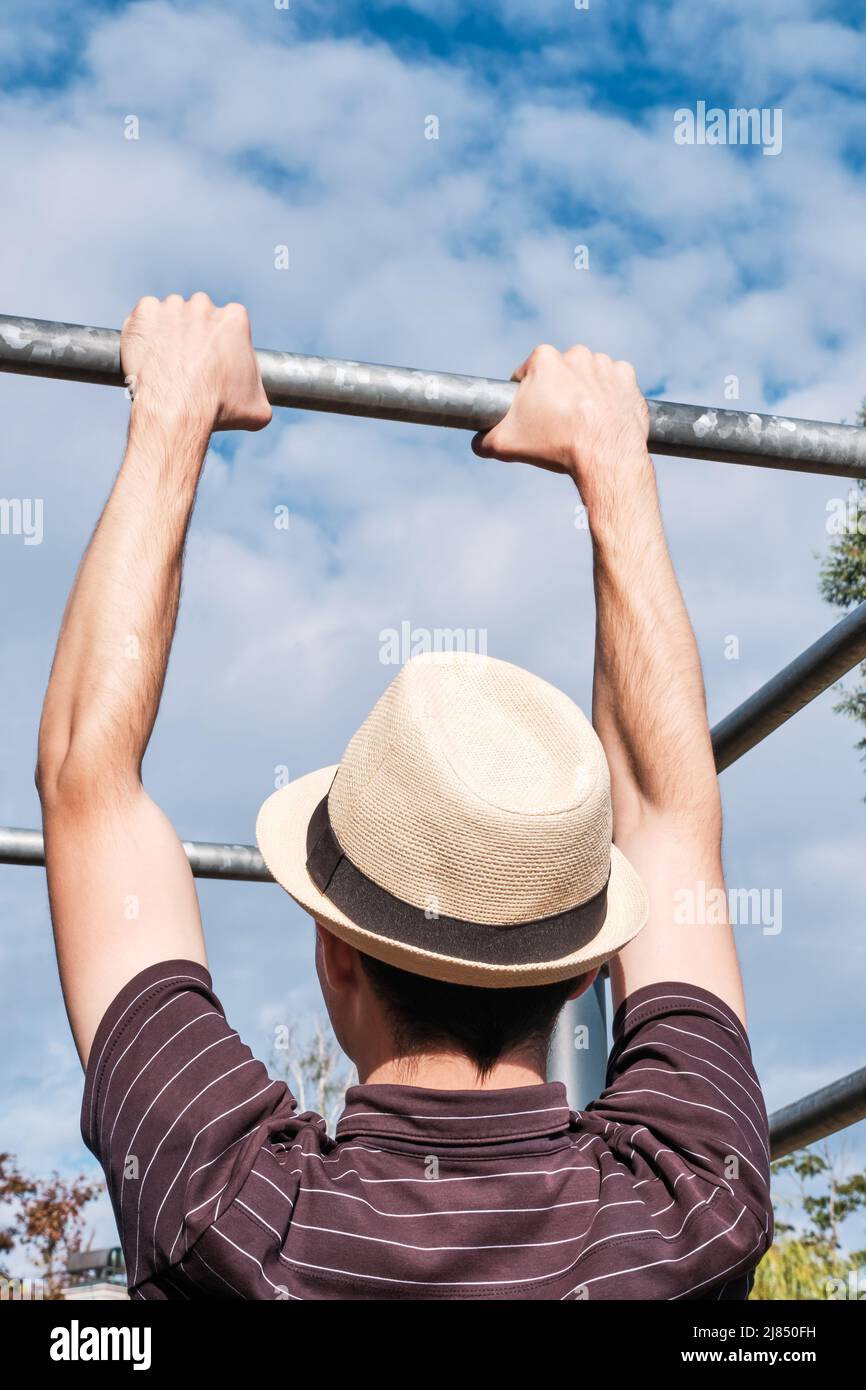 Back view of a young man in a hat pull-up on the bar. Hipster or nerd ...