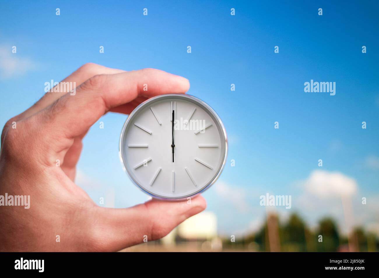 The dial of a watch in a hand against a background of blue sky. Twelve ...