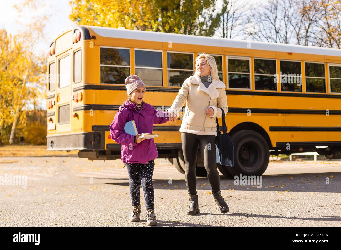 Mother walking her daughter to school bus outside the elementary school ...