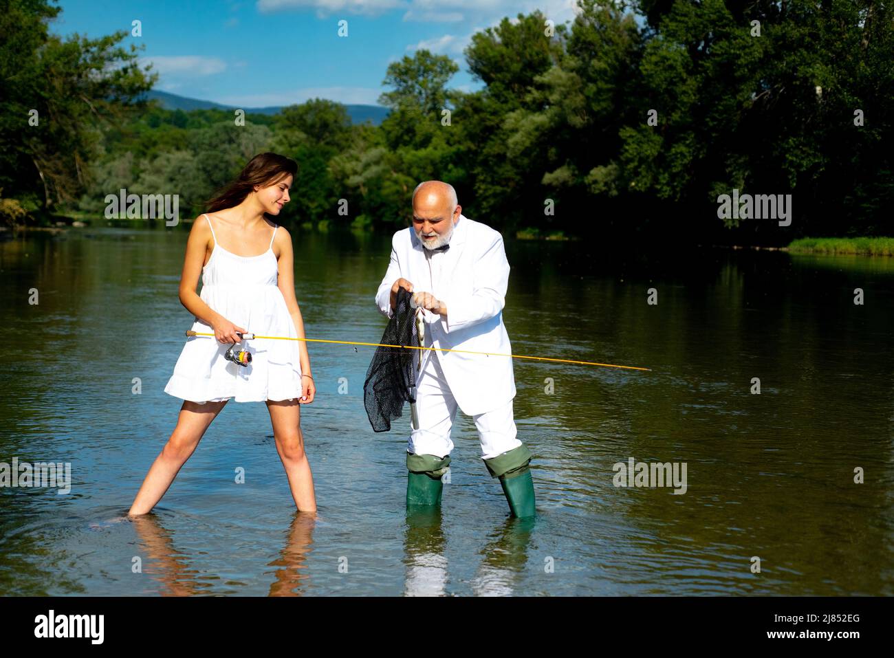 Funny couple of young pretty beauty woman and old fisherman standing in ...