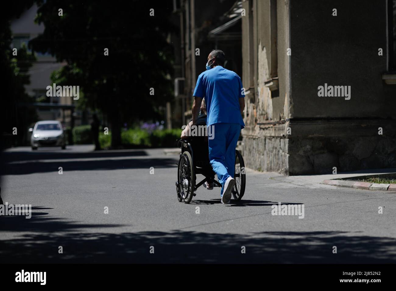 Orderly man pushes a senior male patient in a wheelchair on the ...