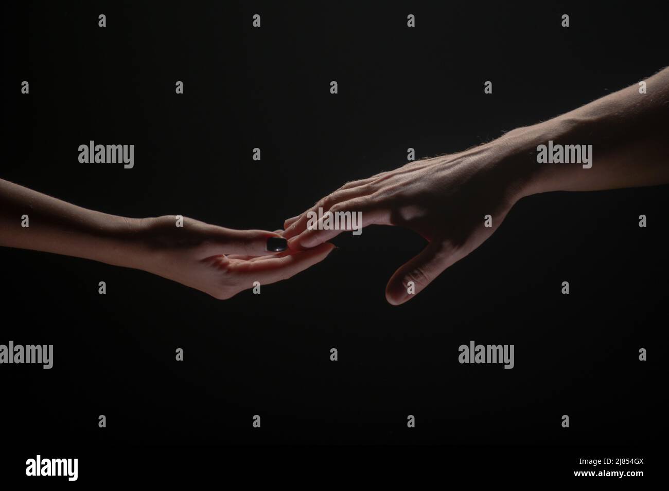 Two hands stretch each other, black background. Couple in love holding hads, close up. Helping ...