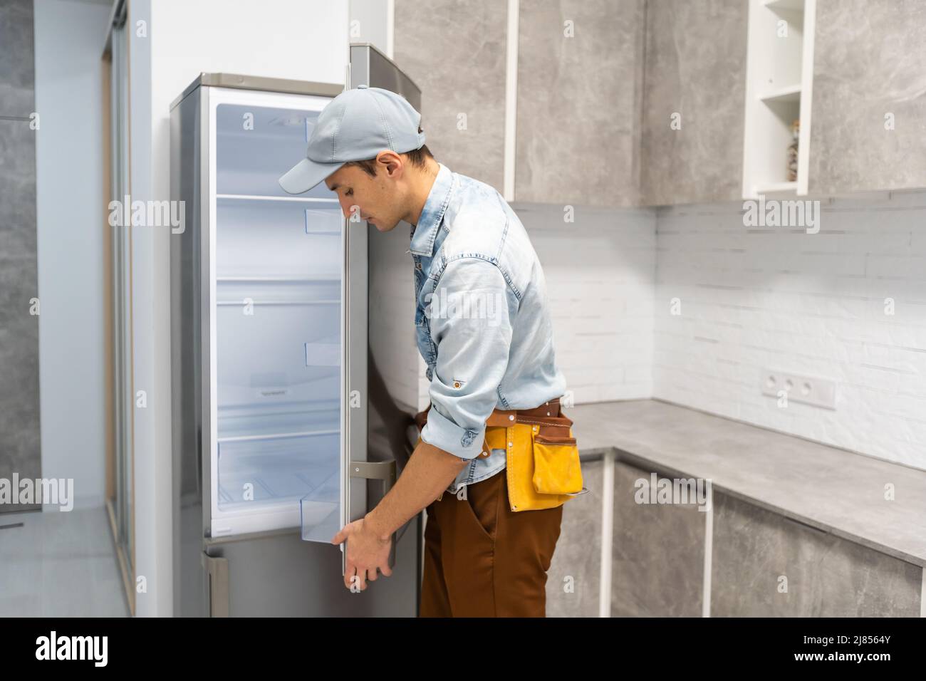 young repairman with tool belt looking at broken refrigerator Stock ...
