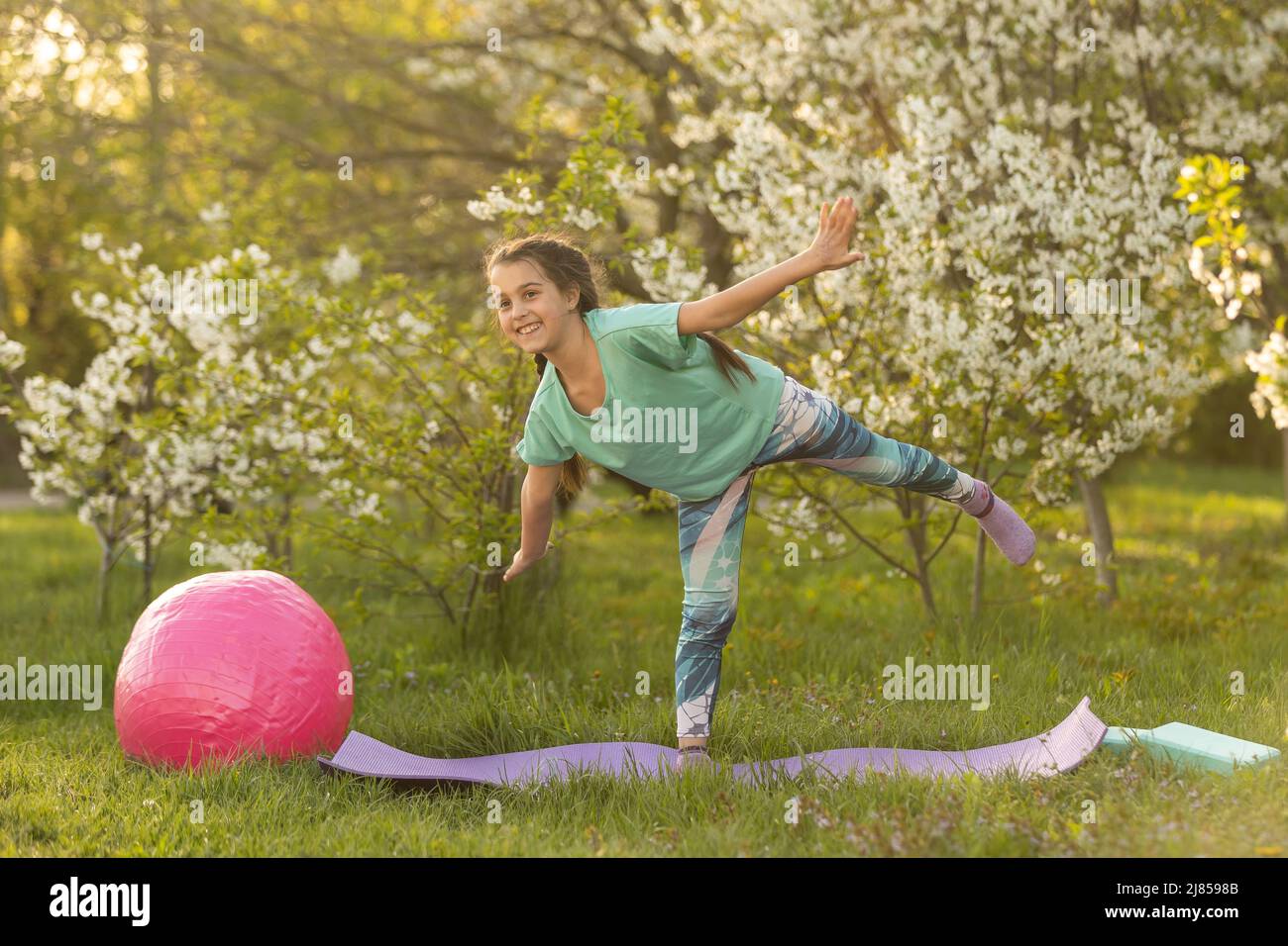 Little girl child doing yoga exercise stretching on the grass in sunny ...