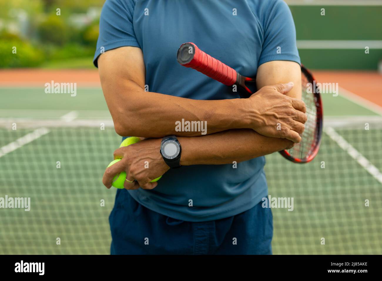 Midsection of biracial senior man with arms crossed holding balls and ...