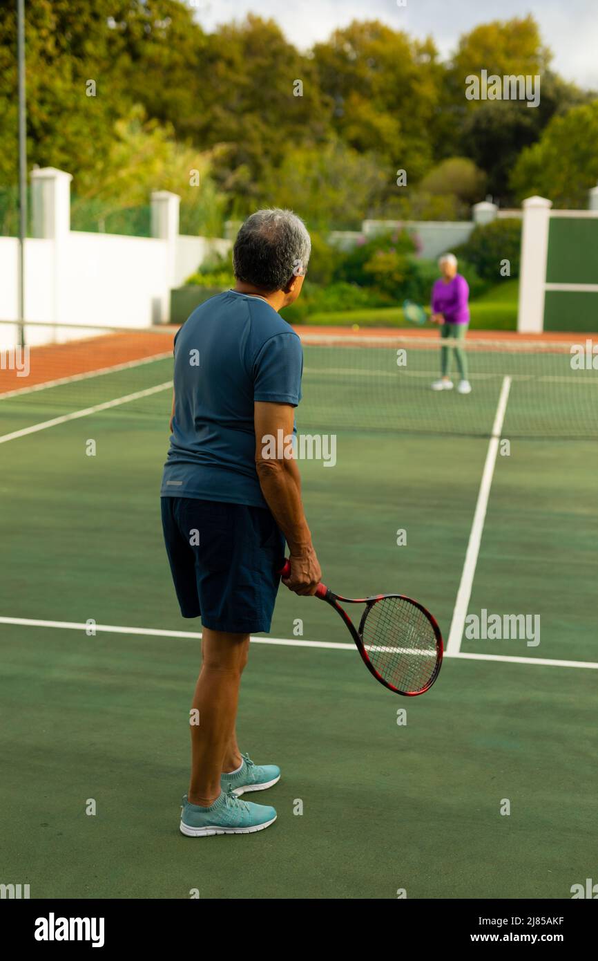 Biracial senior man holding racket playing tennis with senior wife ...