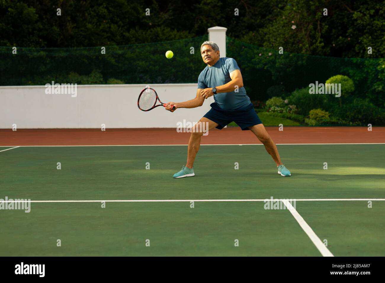 Full length of biracial senior man hitting tennis ball with racket ...