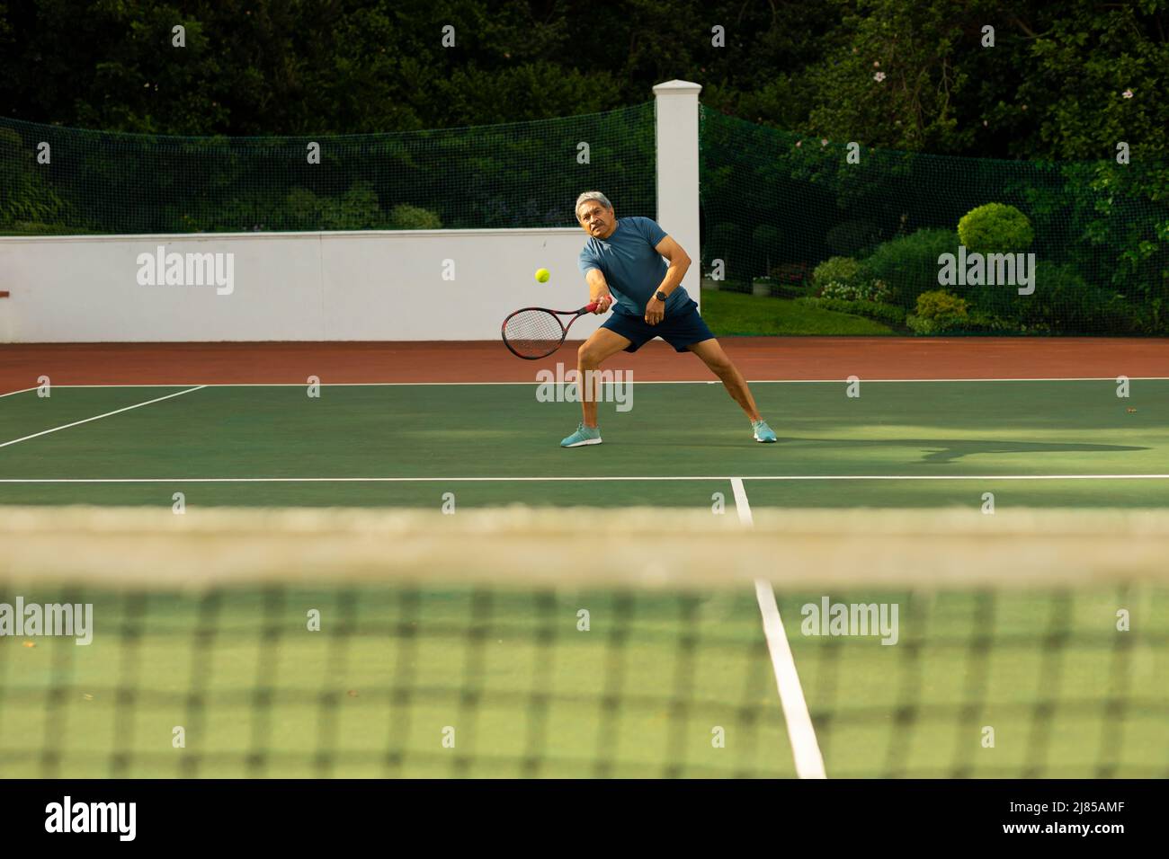 Active biracial senior man hitting tennis ball with racket while ...