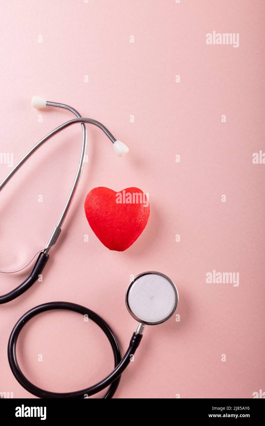 Overhead view of stethoscope with red heart shape against pink ...