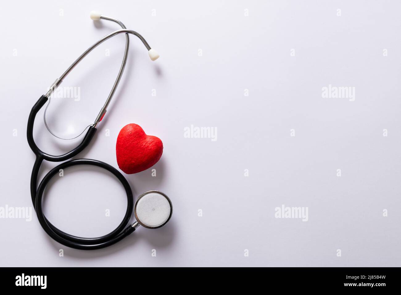 Overhead view of red heart shape and stethoscope against white ...