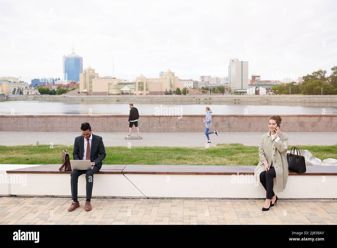 Busy people sitting on bench in city park and working outside keeping ...