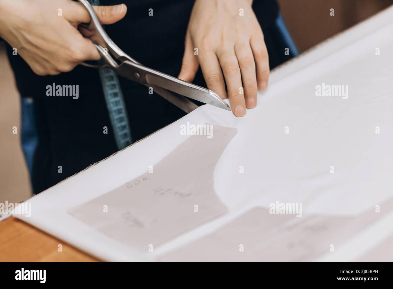 The tailor cuts out the fabric according to the pattern, close up ...