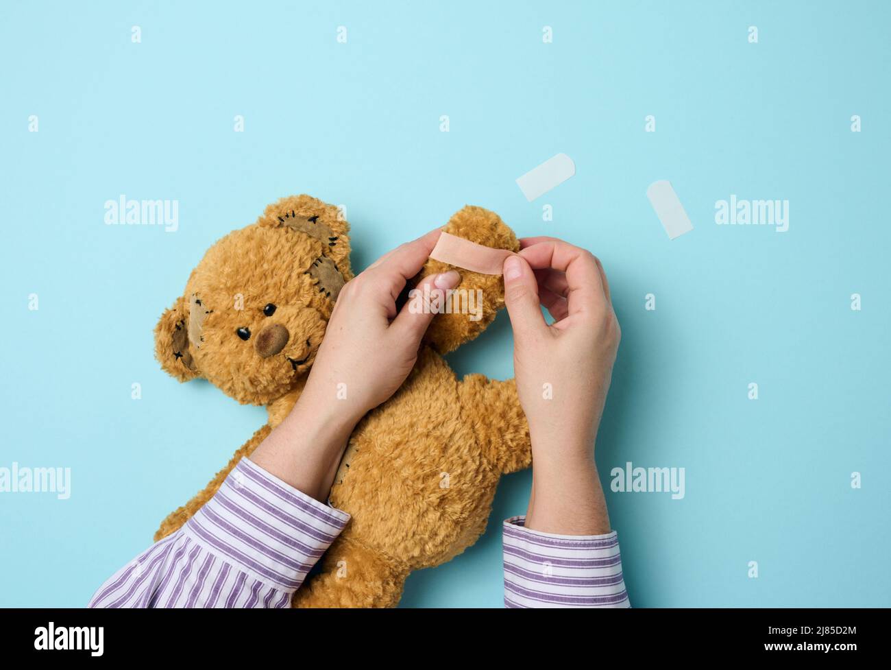 female hand holds a brown teddy bear and glues a medical adhesive ...