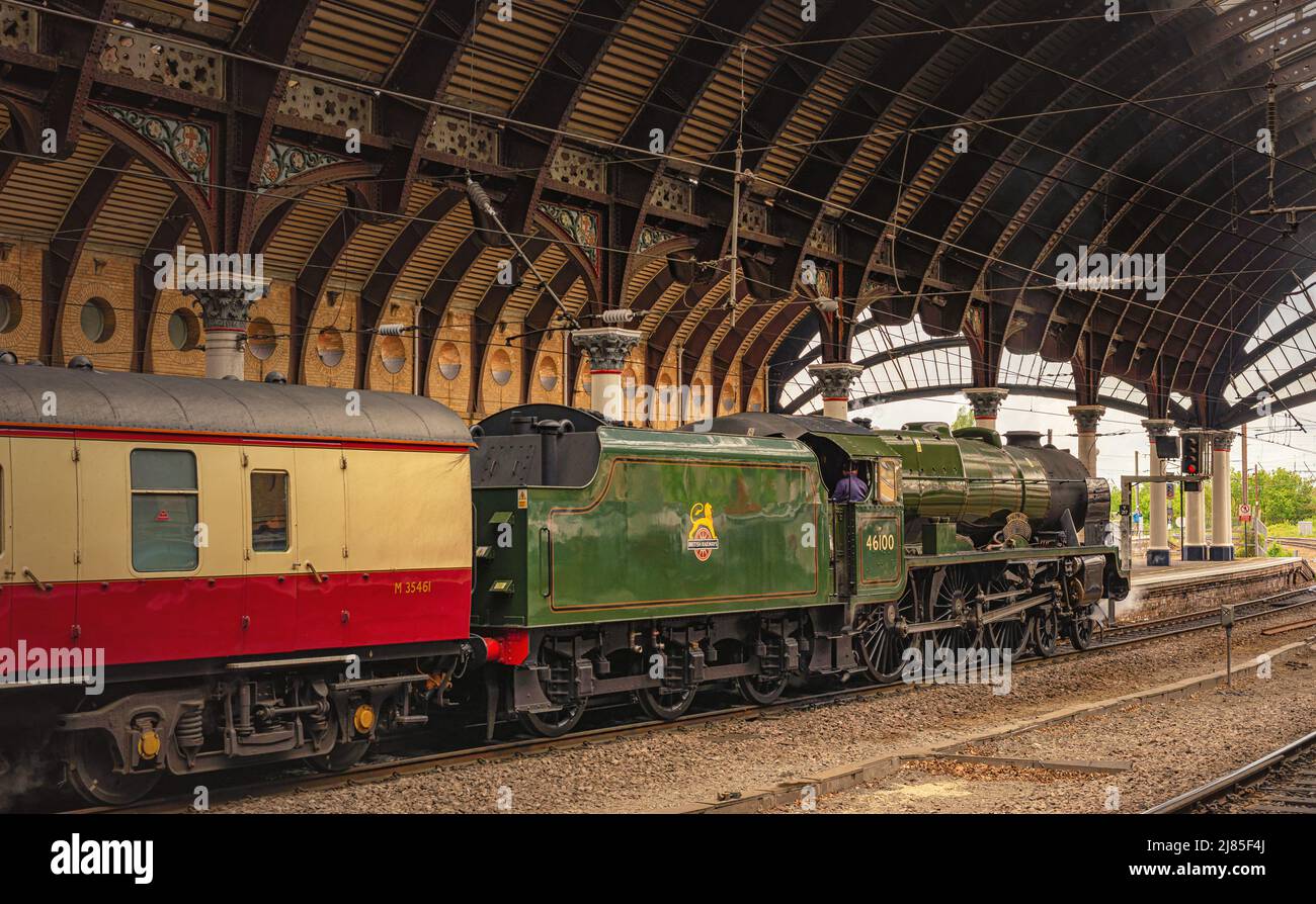 Old steam train stands at a historic railway station platform. A curved ...