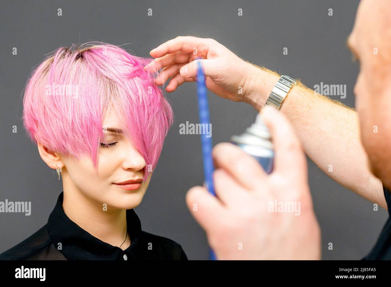 The hairdresser is using hair spray to fix the short pink hairstyle of ...