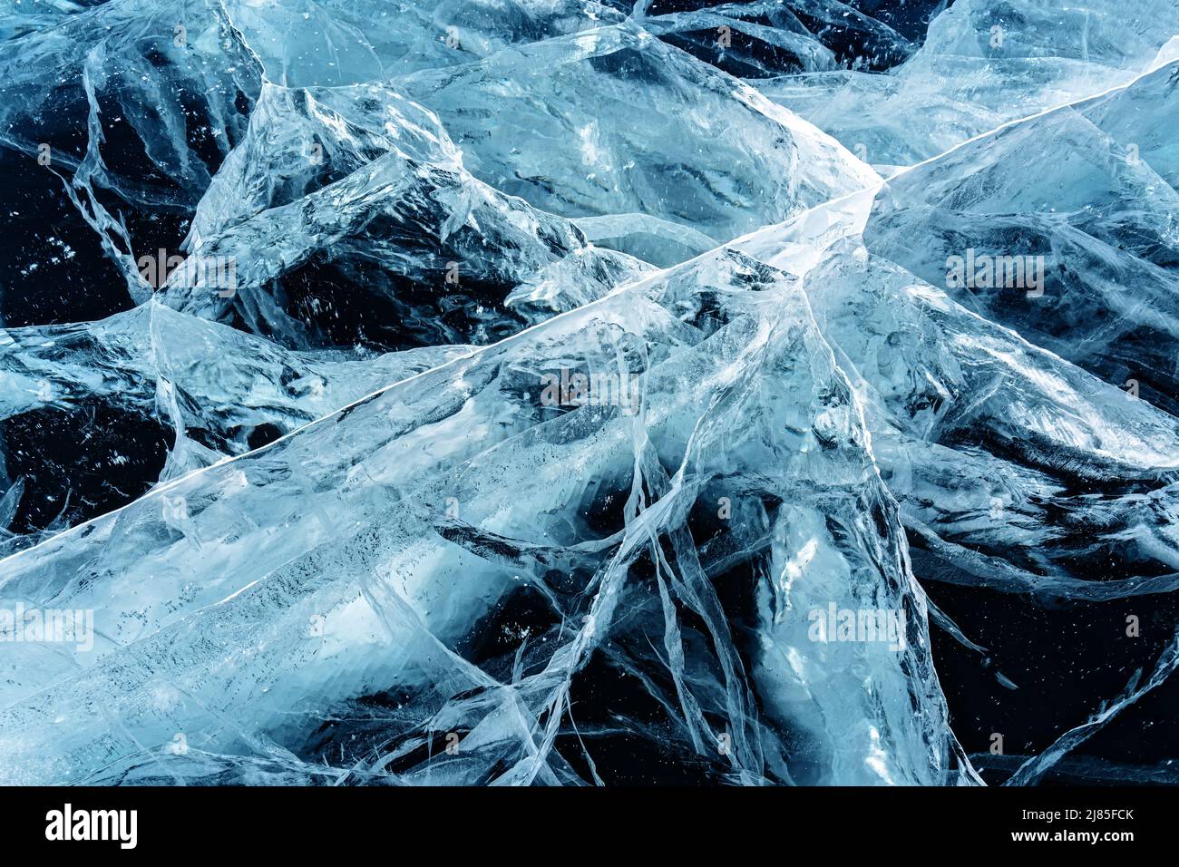 Transparent dark blue ice of frozen Baikal lake with white cracks ...