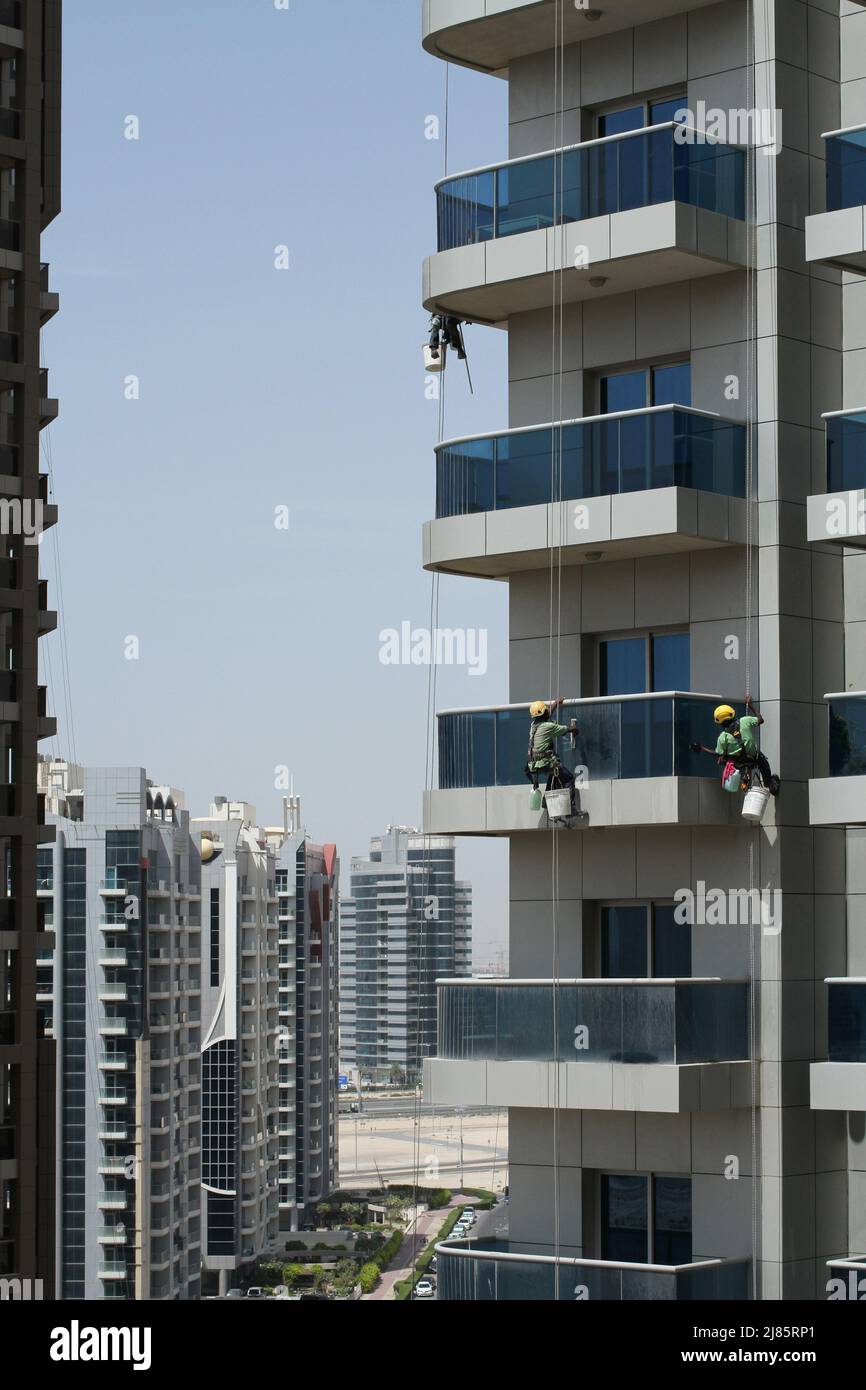 High-rise workers wearing seat belts wash the windows of a high-rise ...
