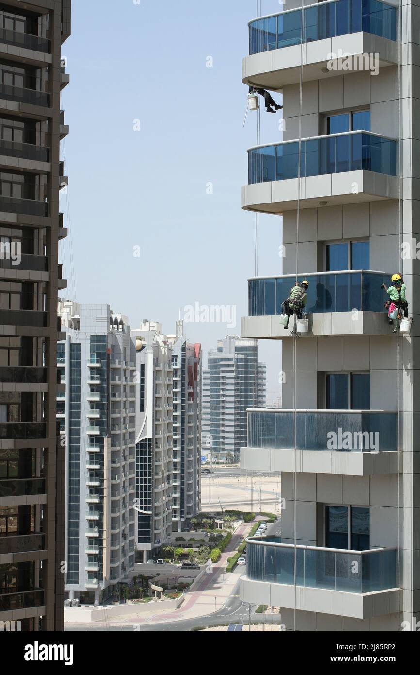 High-rise workers wearing seat belts wash the windows of a high-rise ...