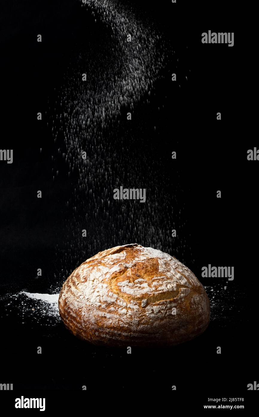 Fresh bread with falling flour on a black background Stock Photo - Alamy