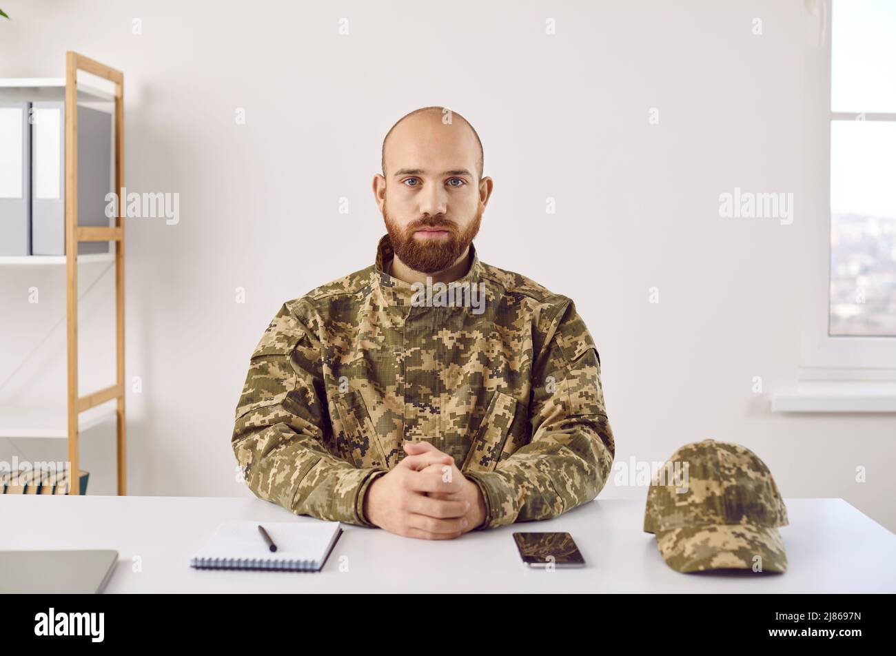 Portrait of serious soldier in camouflage uniform sitting at office ...