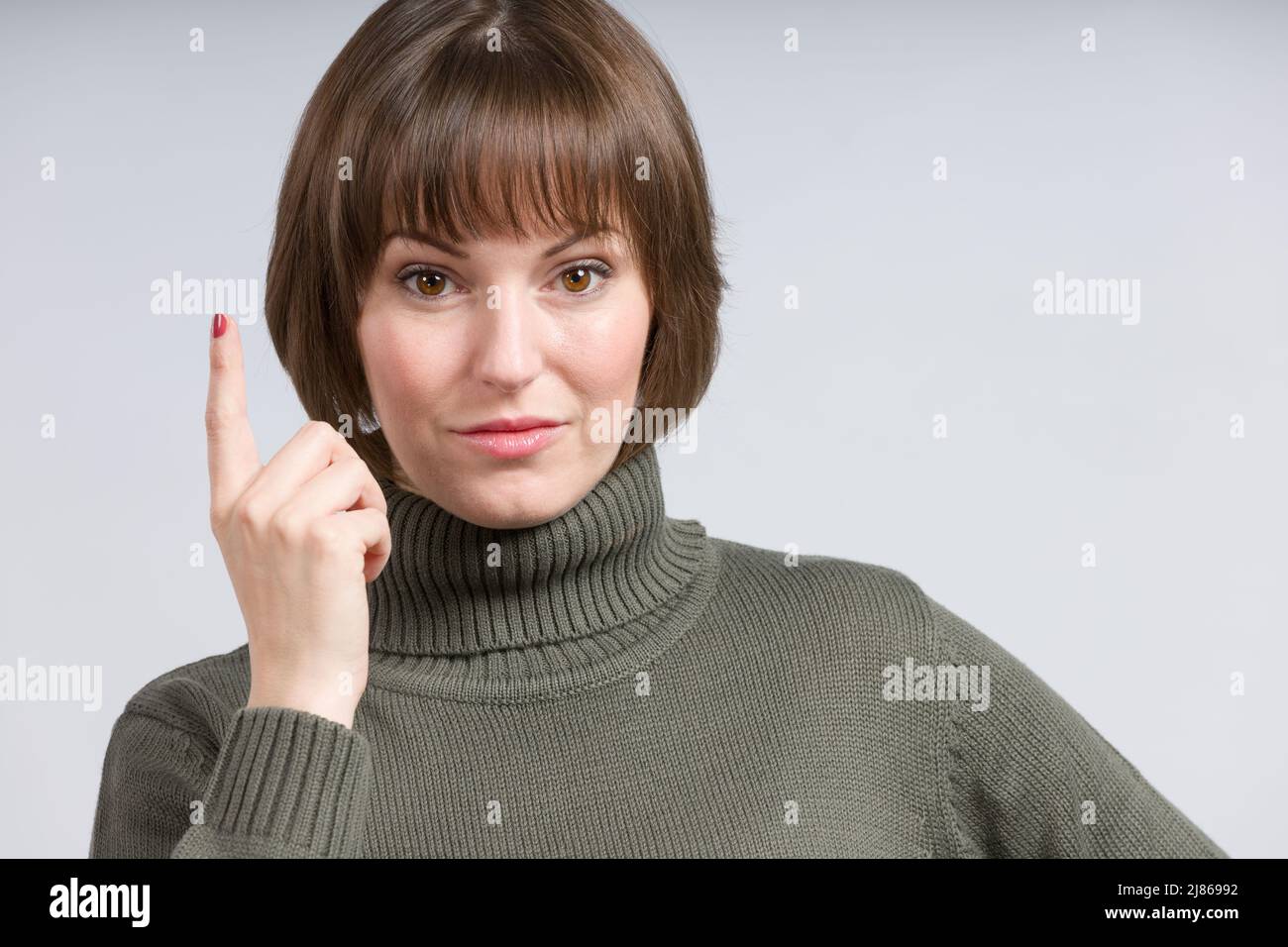 Young smiling / happy woman has an idea an rises her pointer finger ...