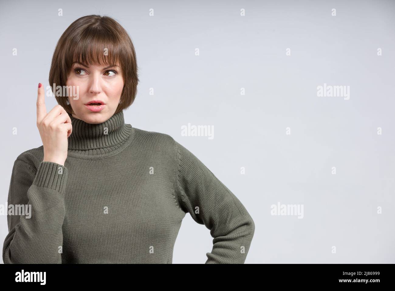 Young smiling / happy woman has an idea an rises her pointer finger ...