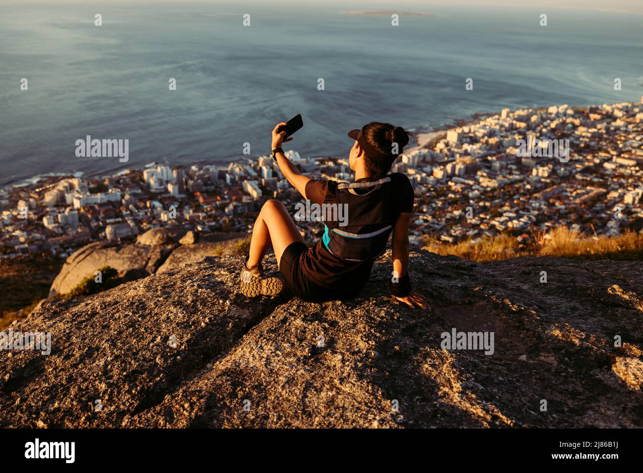 Rear view of female trail runner relaxing on the top of the mountain at ...