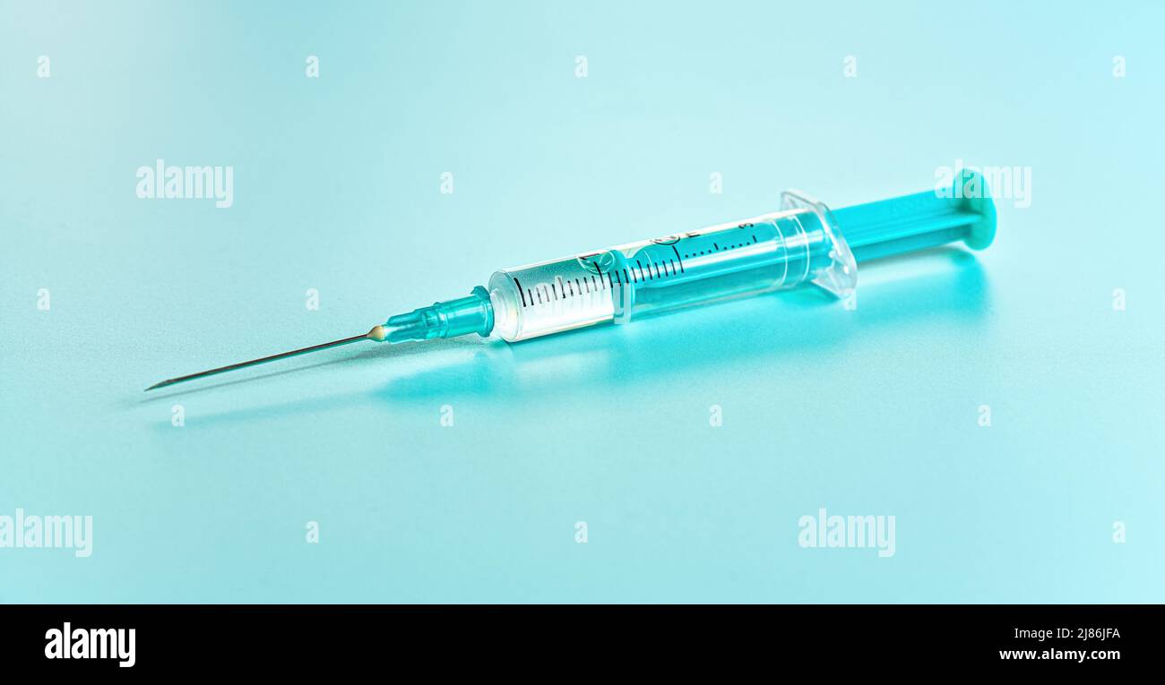 Cyan coloured injection syringe and needle with clear liquid on a board ...