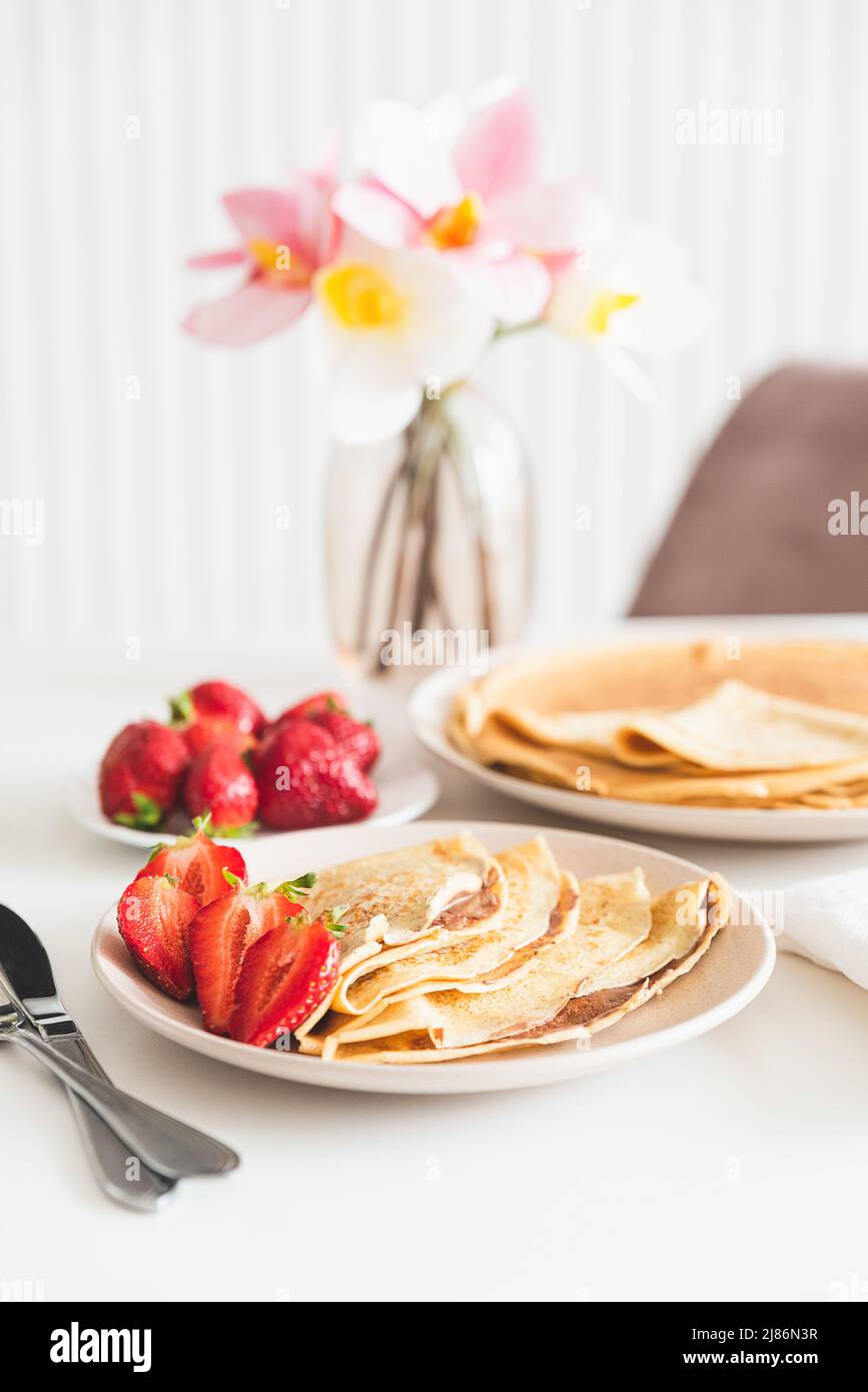 French crepes with chocolate spread and strawberries on white table ...