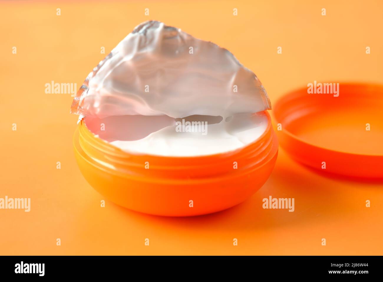 cream in a orange color container on orange background Stock Photo - Alamy