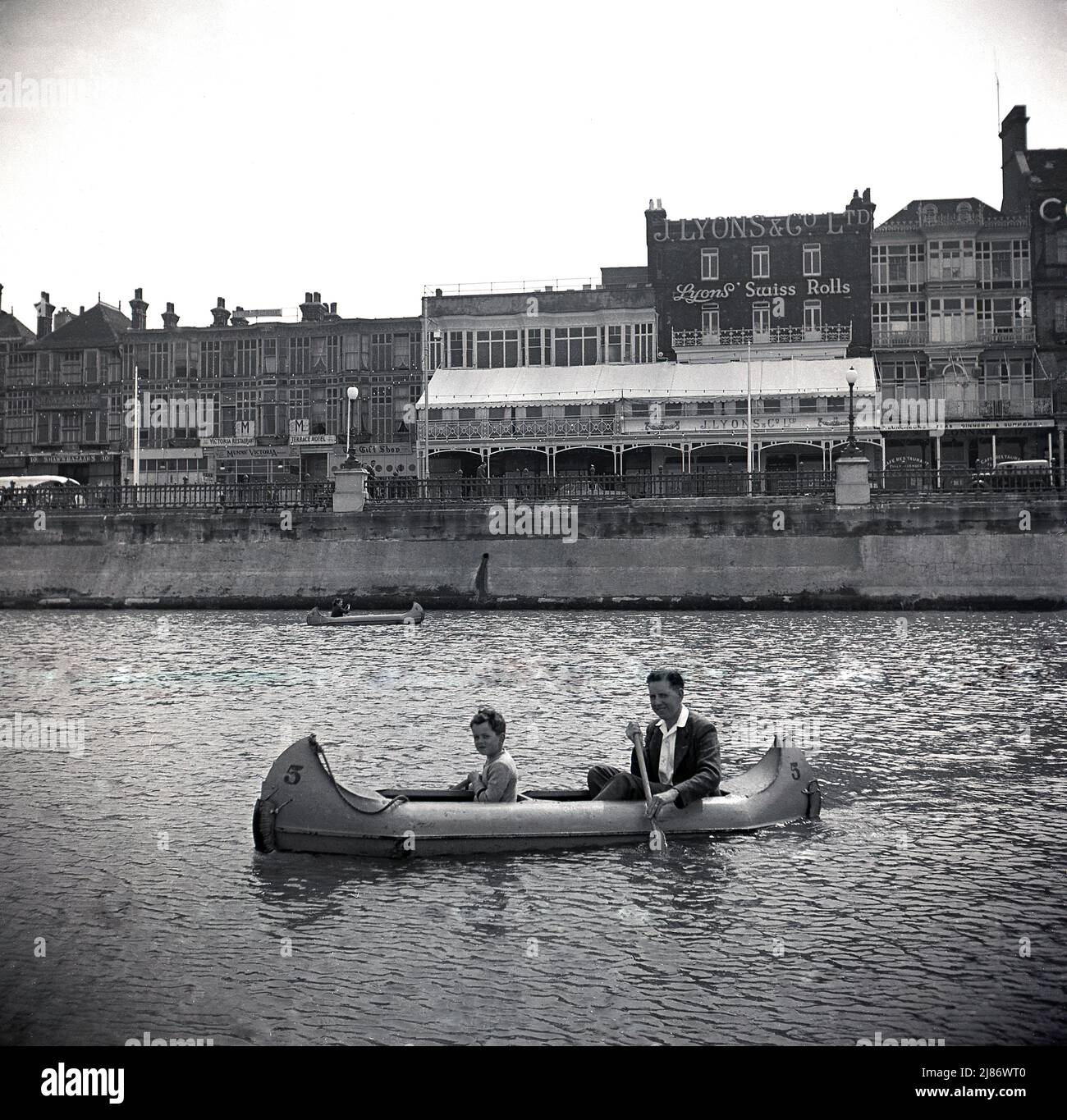 1950s, historical, a father and son in a canoe on the calm sea at ...