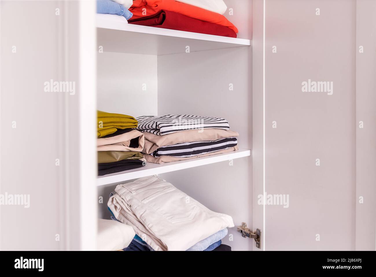 Close-up of an order in a white closet with a pile of folded clothes ...
