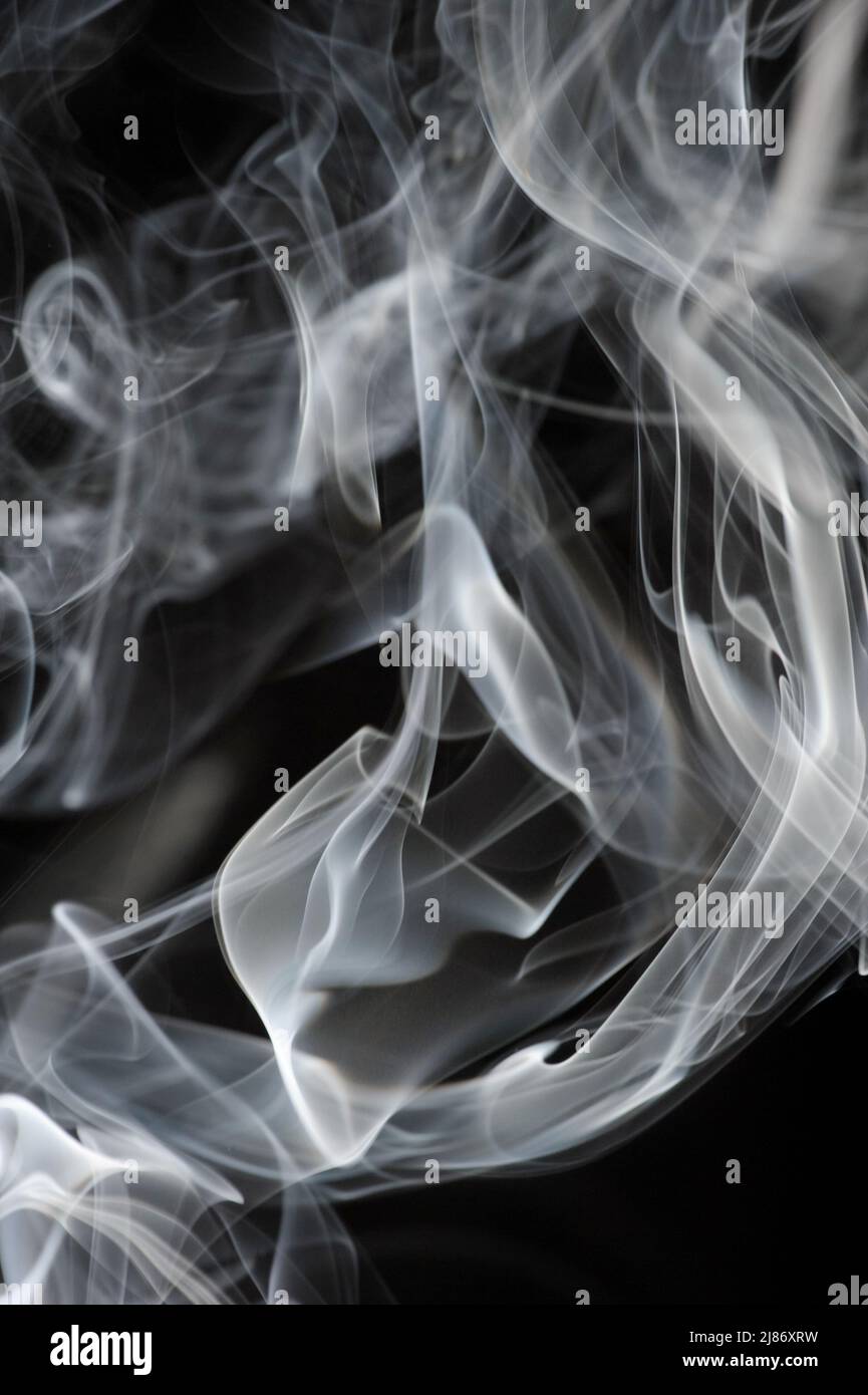 Puffs and curls of white smoke against a black background rising from a ...