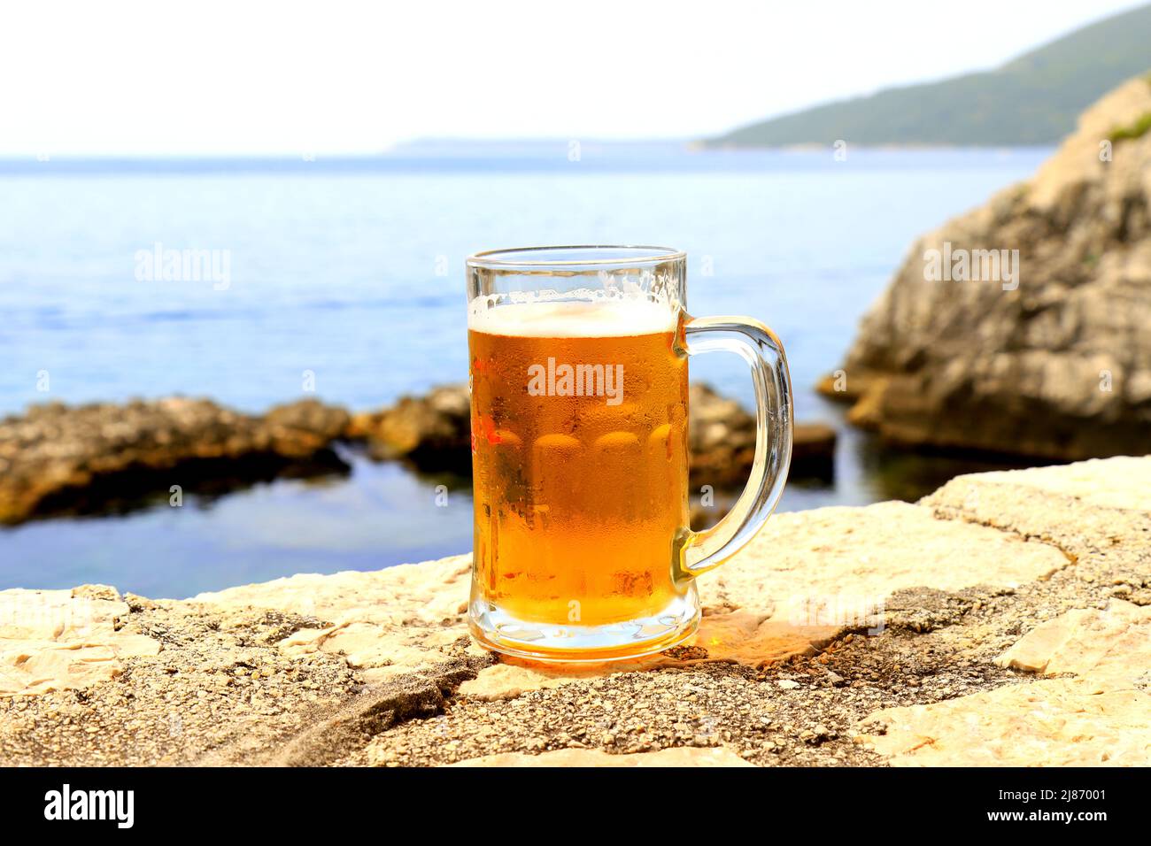 Glass of light beer near sea, close-up. Misted mug, pint of cold beer ...