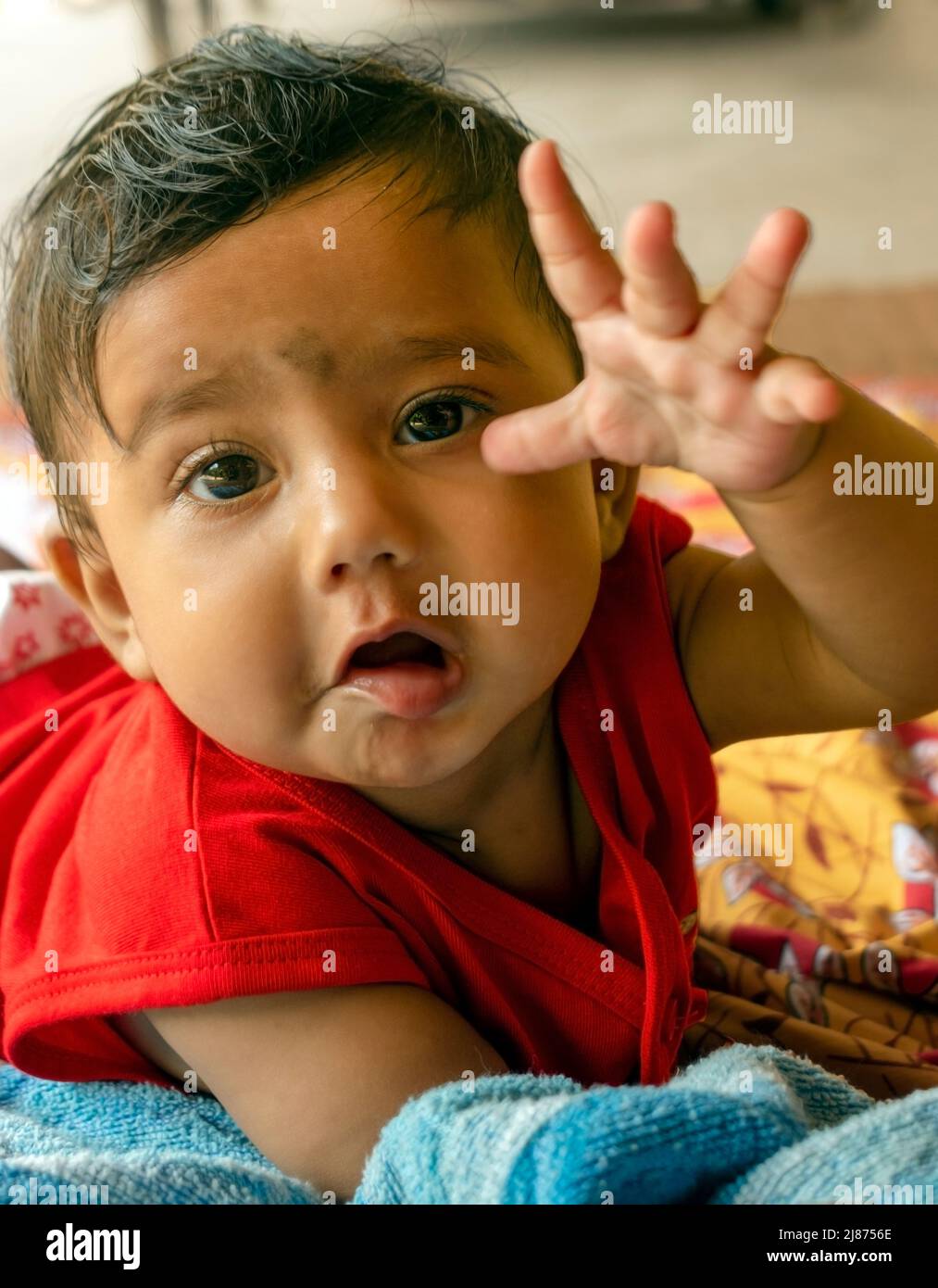 Cute indian baby lying on bed sheet over a mat extending arm towards ...