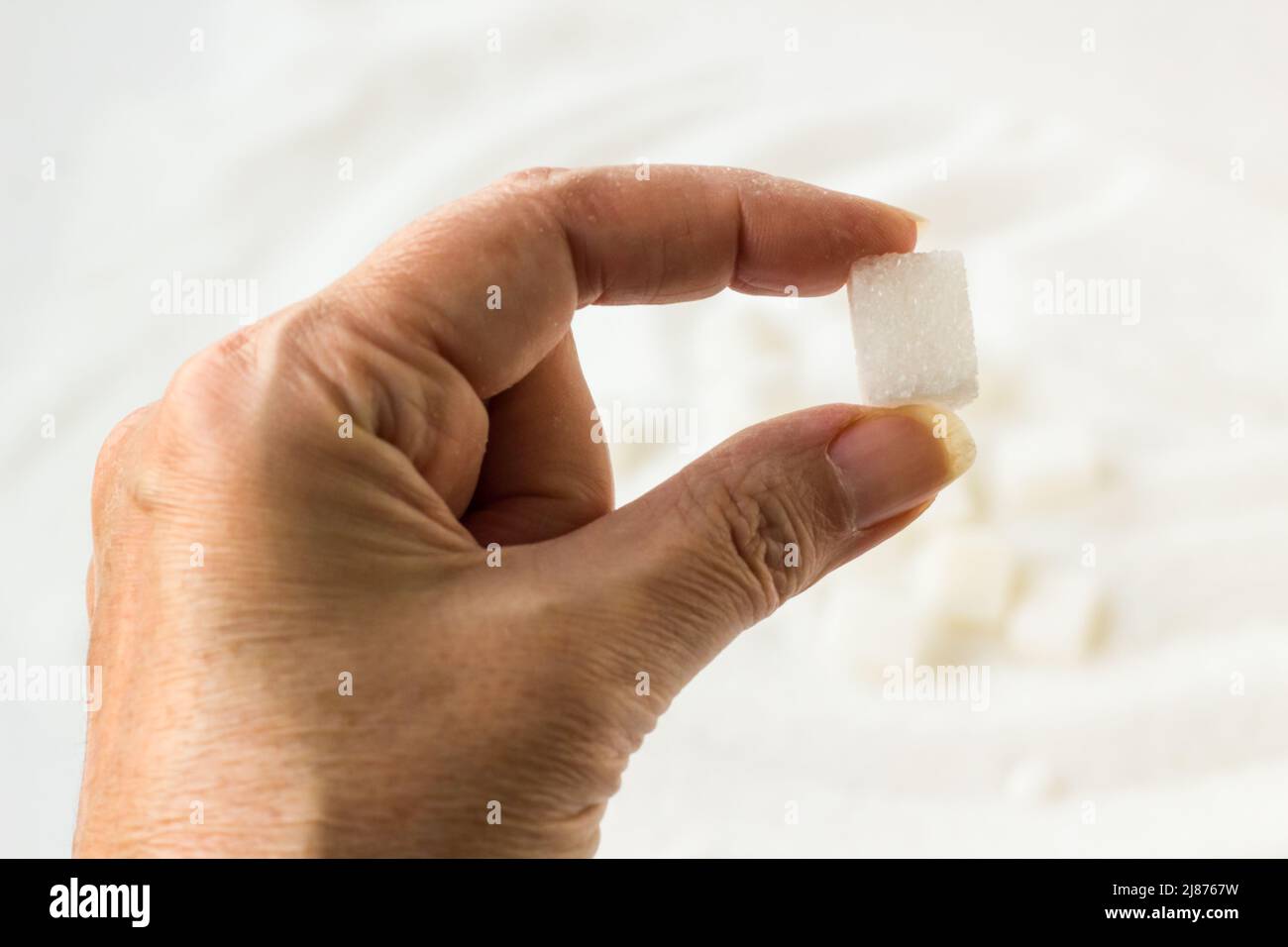 A hand holding a sugar cube,on a granulated sugar background Stock ...