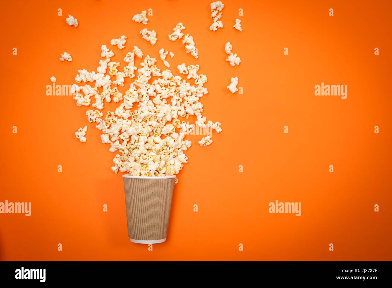 Popcorn spills out of the glass on an orange background, viewed from ...