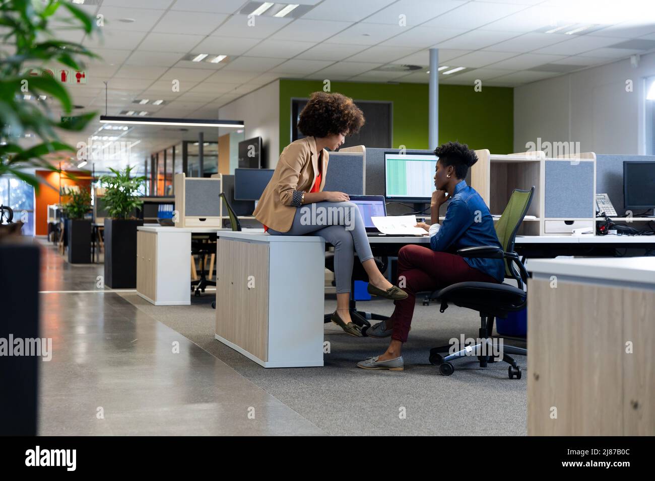 Young multiracial female colleagues discussing over document sitting ...