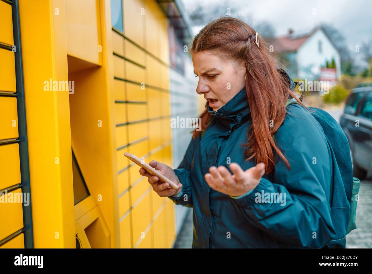 Caucasian angry woman with smartphone app at outdoor automated parcel ...