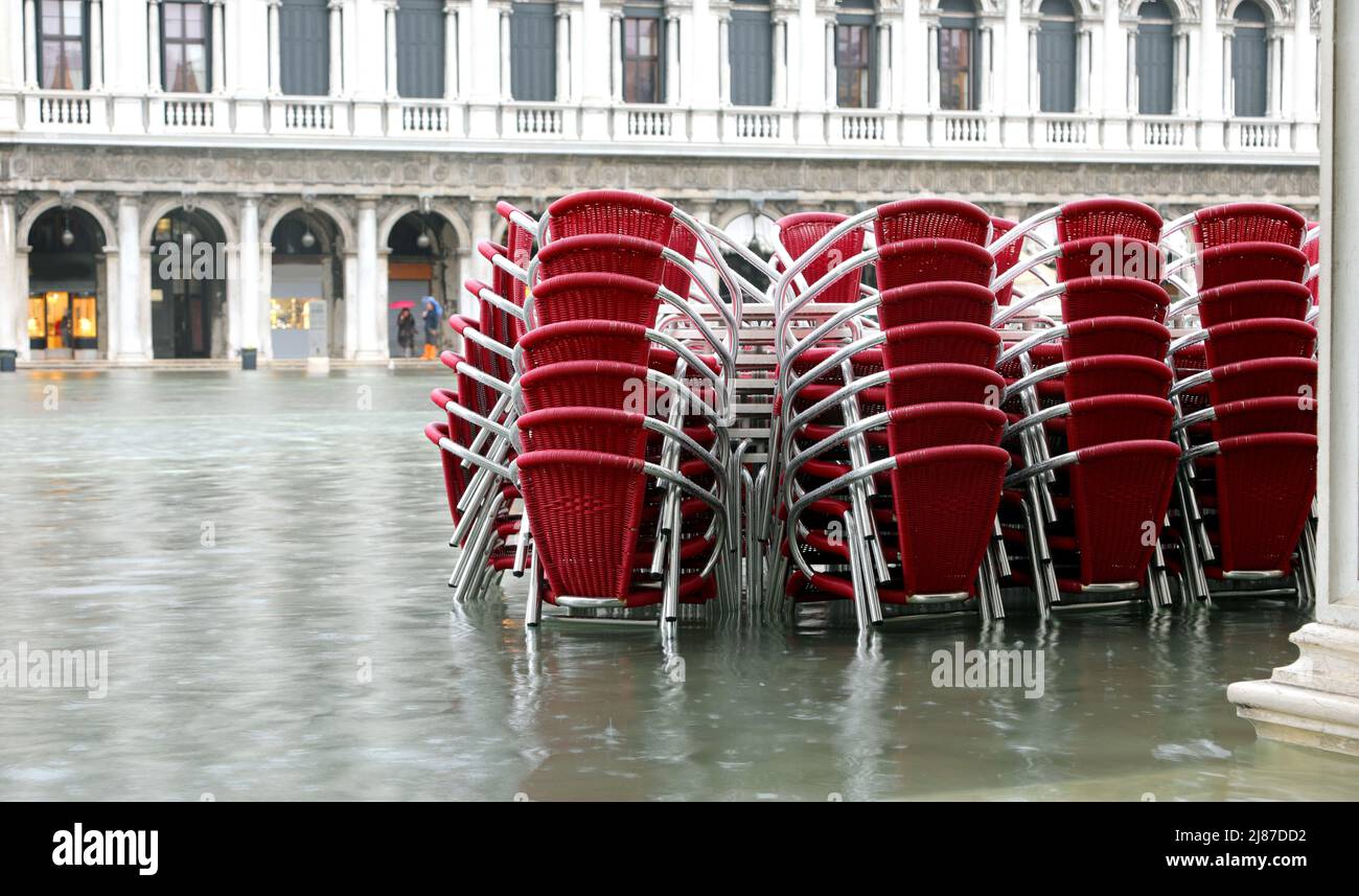 red chairs of the outdoor bar in the flooded Square of Saint Mark during tide in Venice in Italy ...