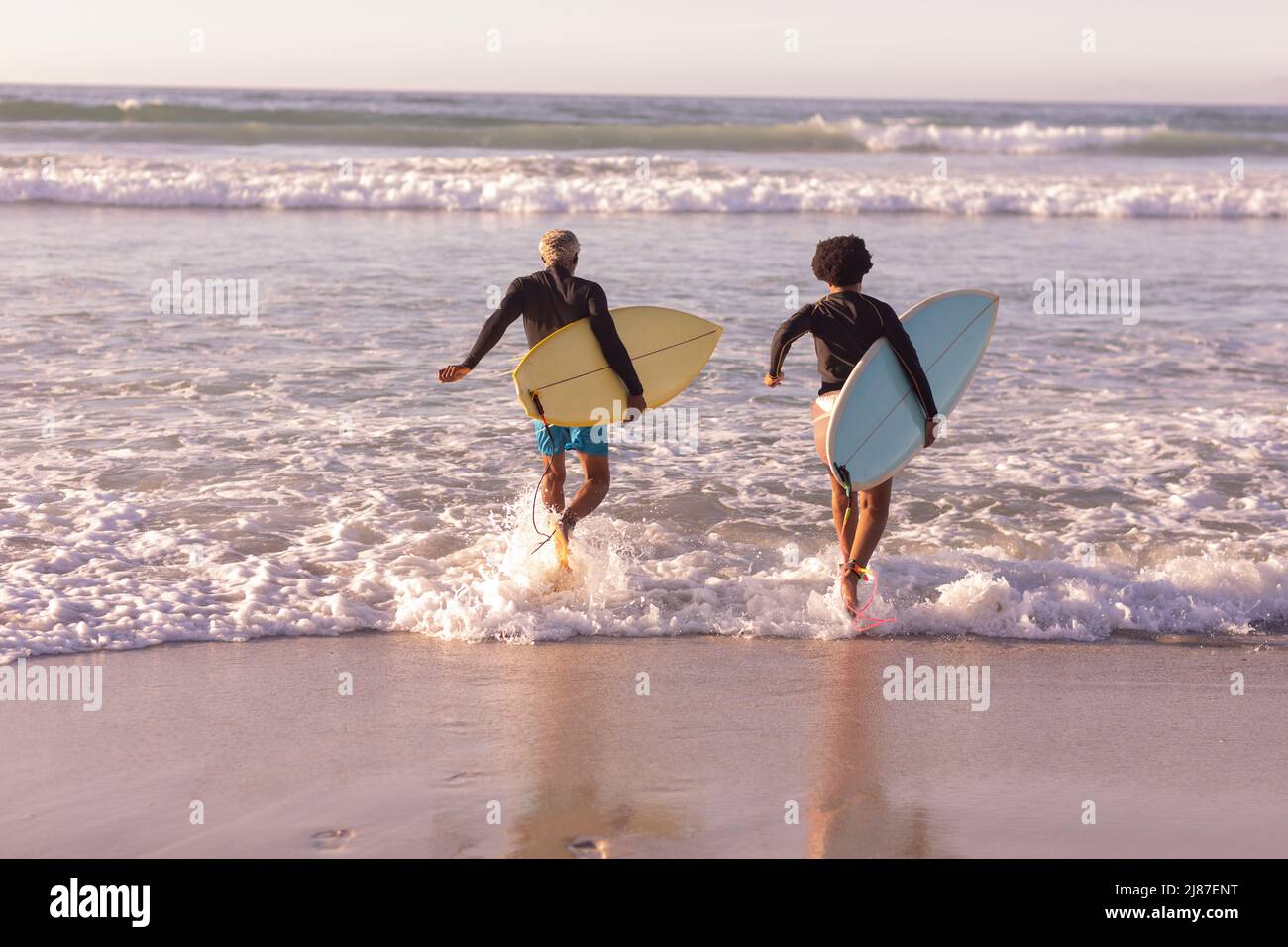 Rear view of african american couple with surfboards running amidst ...