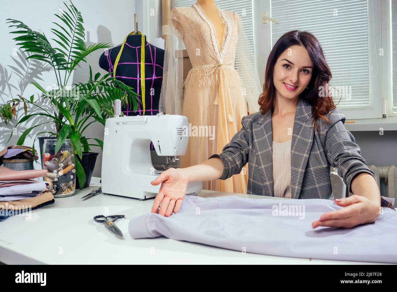 Portrait of a seamstress in in a checkered jacket working in her sewing ...