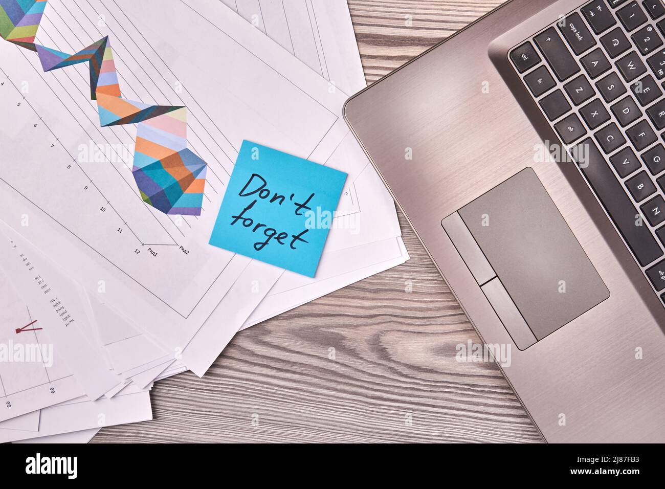 Sticky note with dont forget handwriting with laptop and papers. Charts ...